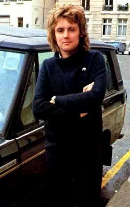 Queen drummer Roger Taylor posing by his car in the 1970s.